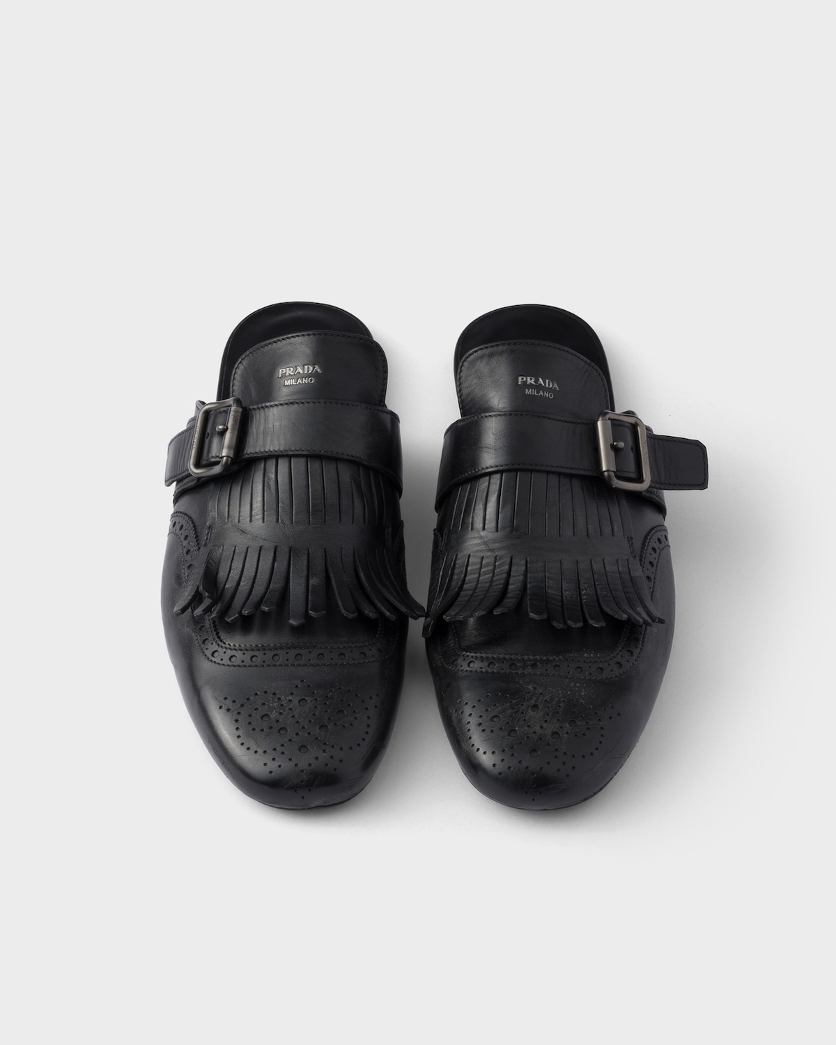 Black Shuffle Antiqued Leather Mules With Buckled Strap And Fringe | PRADA